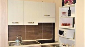 Cozinha compacta com armários brancos, micro-ondas embutido e um pequeno espaço de refeições com mesa e cadeiras brancas.