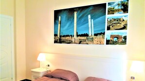 Quarto com duas camas, mesa de cabeceira, um quadro na parede e uma porta.