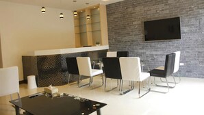 Uma área de jantar moderna com mesa preta, cadeiras brancas e pretas, uma TV de tela plana fixada em uma parede de tijolos e iluminação pendente.