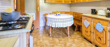 Uma cozinha com armários de madeira, fogão, mesa redonda com toalha de renda e painel de azulejos.