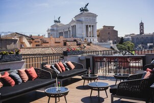 Terraço no telhado com assentos ao ar livre, vista de um edifício histórico e uma torre do relógio ao fundo.