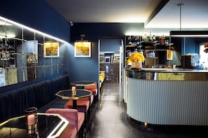 Uma área de bar com assentos, um balcão com garrafas e vista para o salão.