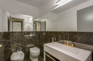 Uma casa de banho moderna com bidé, sanita e um espelho grande.