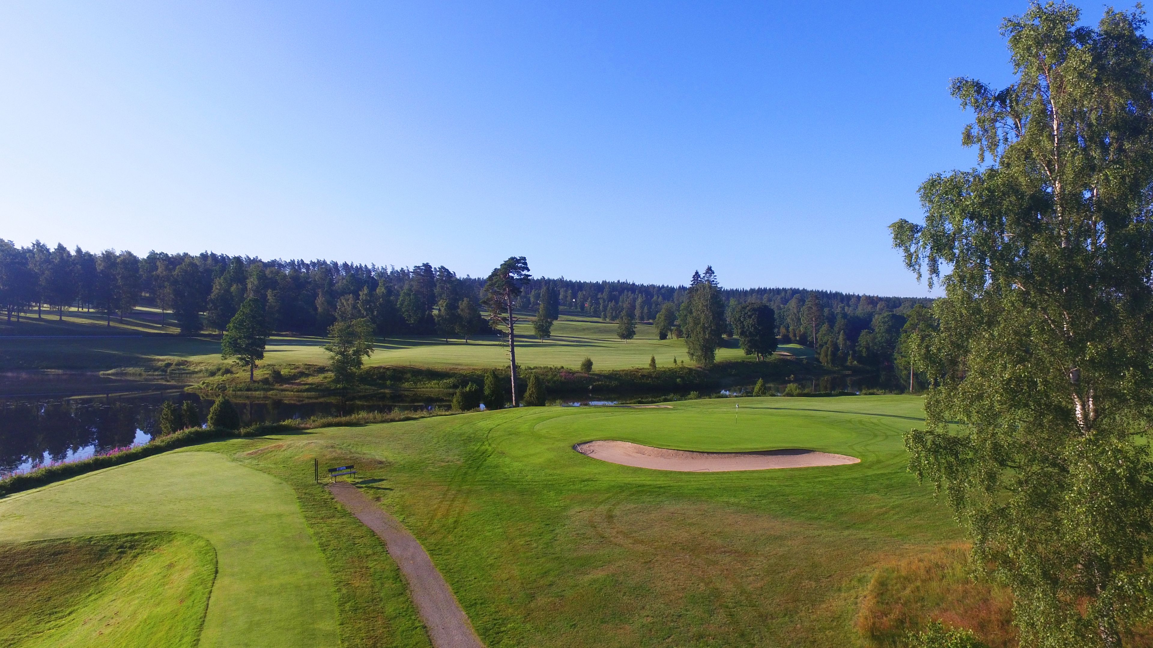 Um campo de golfe com lago, árvores e céu claro.