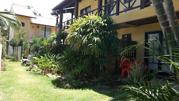 Um pátio com um edifício amarelo, uma varanda de madeira e diversas plantas.