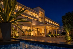 Um hotel moderno com piscina, vários andares e uma entrada bem iluminada.