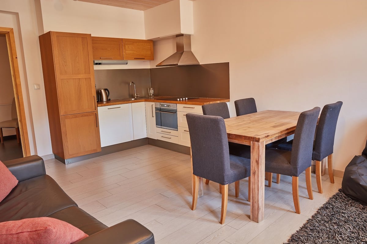 Cozinha moderna com armários de madeira, coifa de aço inoxidável e área de jantar com mesa de madeira e seis cadeiras.