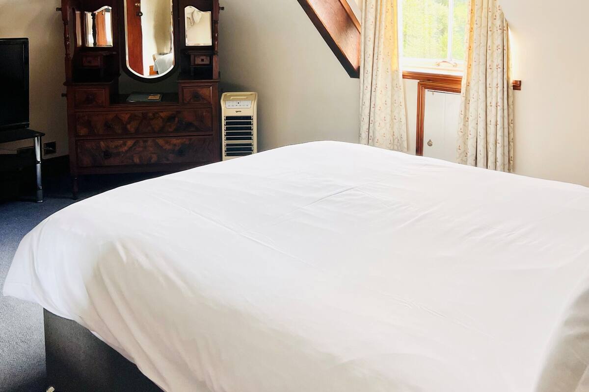Quarto com cama grande, penteadeira com espelho, aquecedor e janela com cortinas.