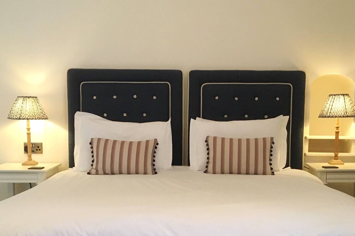 Uma cama de casal com cabeceira escura, duas mesas de cabeceira com abajures e almofadas listradas.