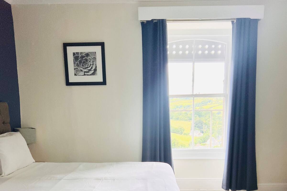 Quarto com uma cama grande, um quadro na parede e uma janela com cortinas.