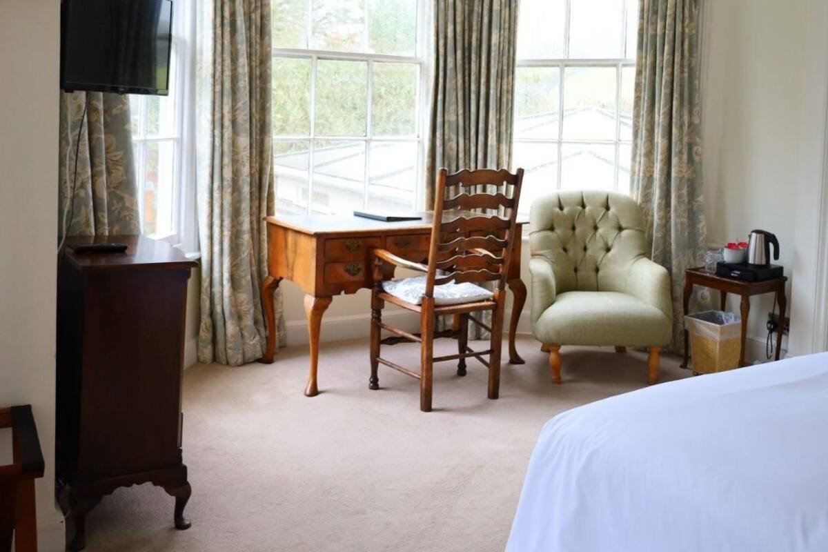 Quarto de hotel com uma cama grande, uma escrivaninha com cadeira, televisão e vista para o exterior através de amplas janelas.