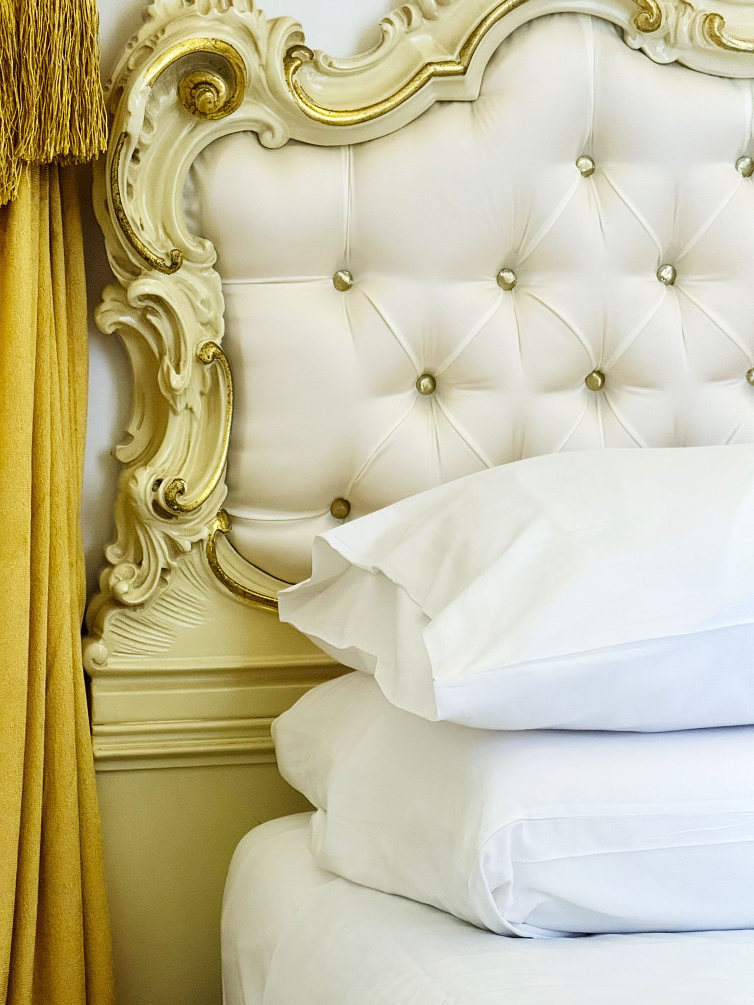 Cama com cabeceira estofada e roupa de cama branca.
