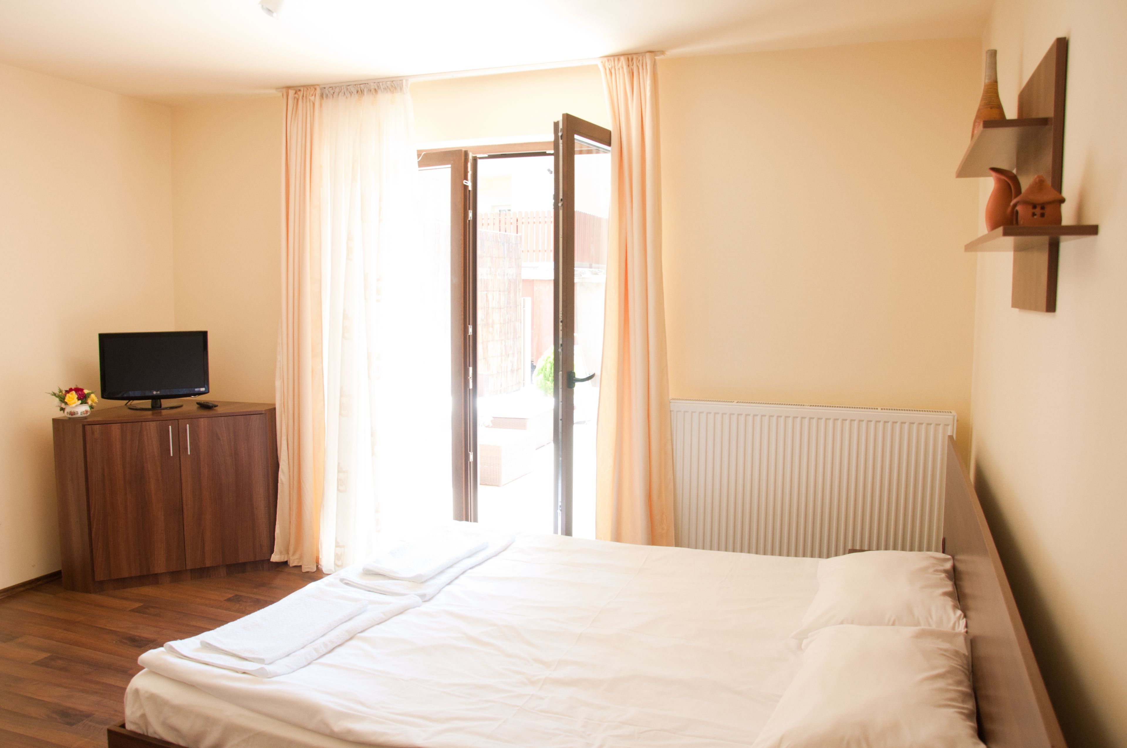 Quarto de hotel com uma cama, uma televisão sobre um móvel de madeira e uma porta de vidro deslizante para uma área externa.