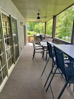Um alpendre coberto com mesa e cadeiras, ventilador de teto e vista para o verde.