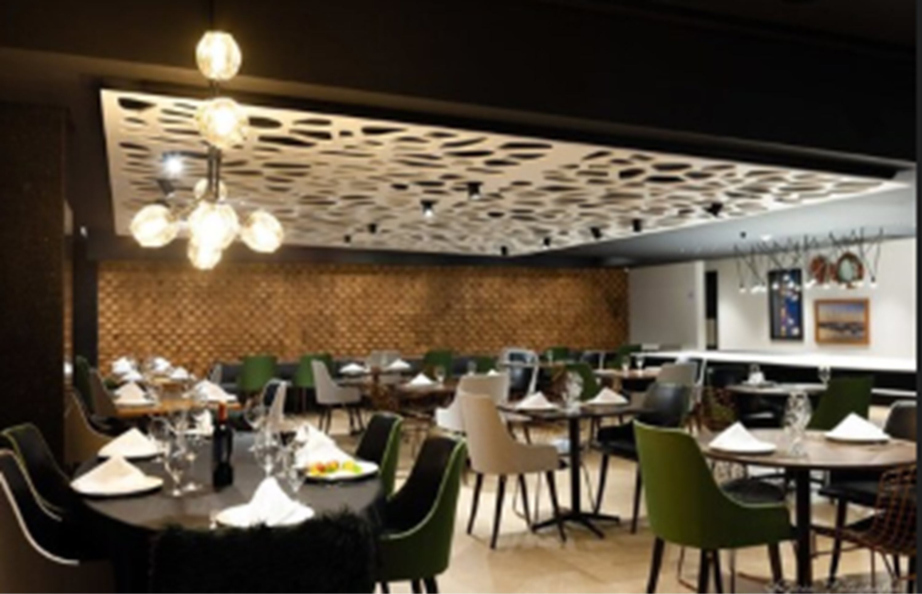 Restaurante com mesas redondas e cadeiras verdes, teto decorativo e parede estampada.