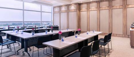 Sala de conferências com mesas, cadeiras e uma grande janela com vista.
