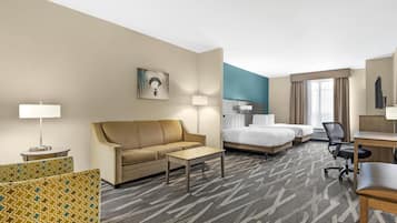Quarto de hotel com sofá, duas camas, escrivaninha e tapete estampado.