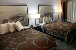 Quarto de hotel com duas camas, uma mesa de cabeceira, um abajur e um quadro grande na parede.