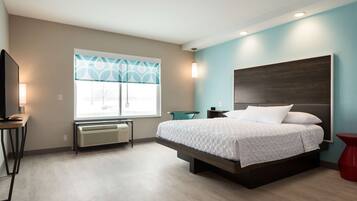 Quarto de hotel moderno com cama, escrivaninha, cadeira e televisão.