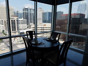 Uma sala de jantar com uma mesa redonda e cadeiras, grandes janelas com vista para a cidade.