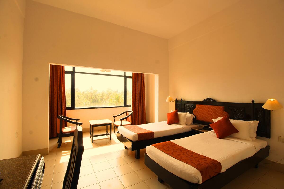 Quarto de hotel com duas camas, uma escrivaninha, cadeiras e uma janela com cortinas.
