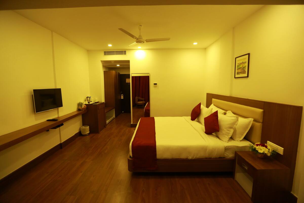 Quarto de hotel com cama, mesa de cabeceira, televisão e ventoinha no teto.