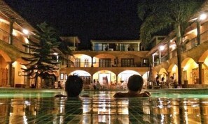 Vista noturna de uma área de piscina com vários níveis de varandas e um espaço aberto central.