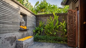 Um pátio tranquilo com uma estátua de Buda, um banco de concreto e uma porta decorativa.