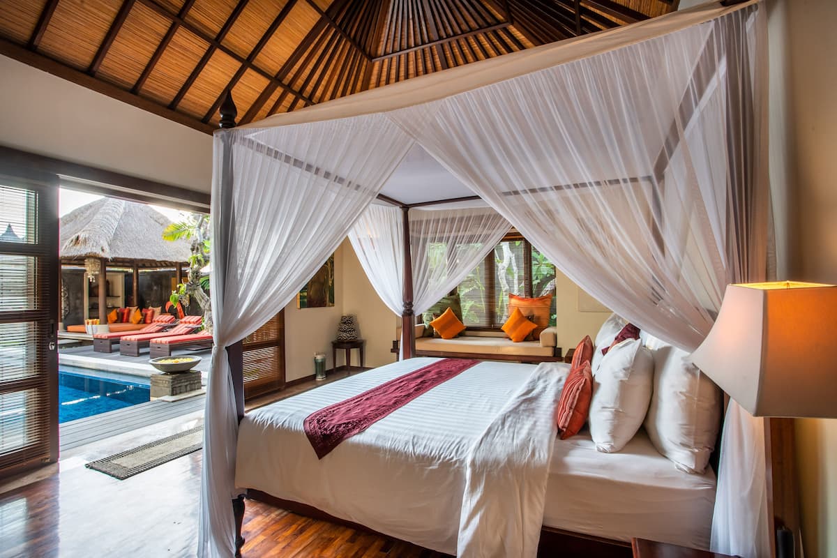 Um quarto espaçoso com uma cama grande, um dossel e vista para uma piscina ao ar livre.