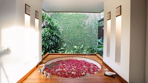 Uma área de spa com um banco de madeira, uma banheira cheia de pétalas de rosa e uma parede coberta de vegetação.