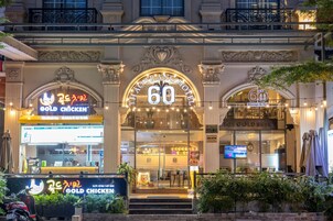Fachada de hotel com um grande letreiro "60", um restaurante "Gold Chicken" e um serviço de "Massagem & Spa".