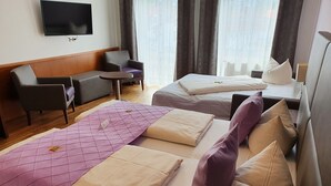 Quarto de hotel com duas camas, um sofá, uma mesinha e uma televisão na parede.