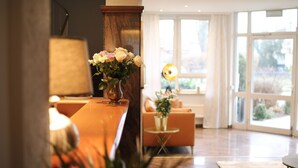 Uma sala de estar moderna com uma mesa de centro de madeira, um vaso com flores, um sofá e uma janela grande com vista para o verde.