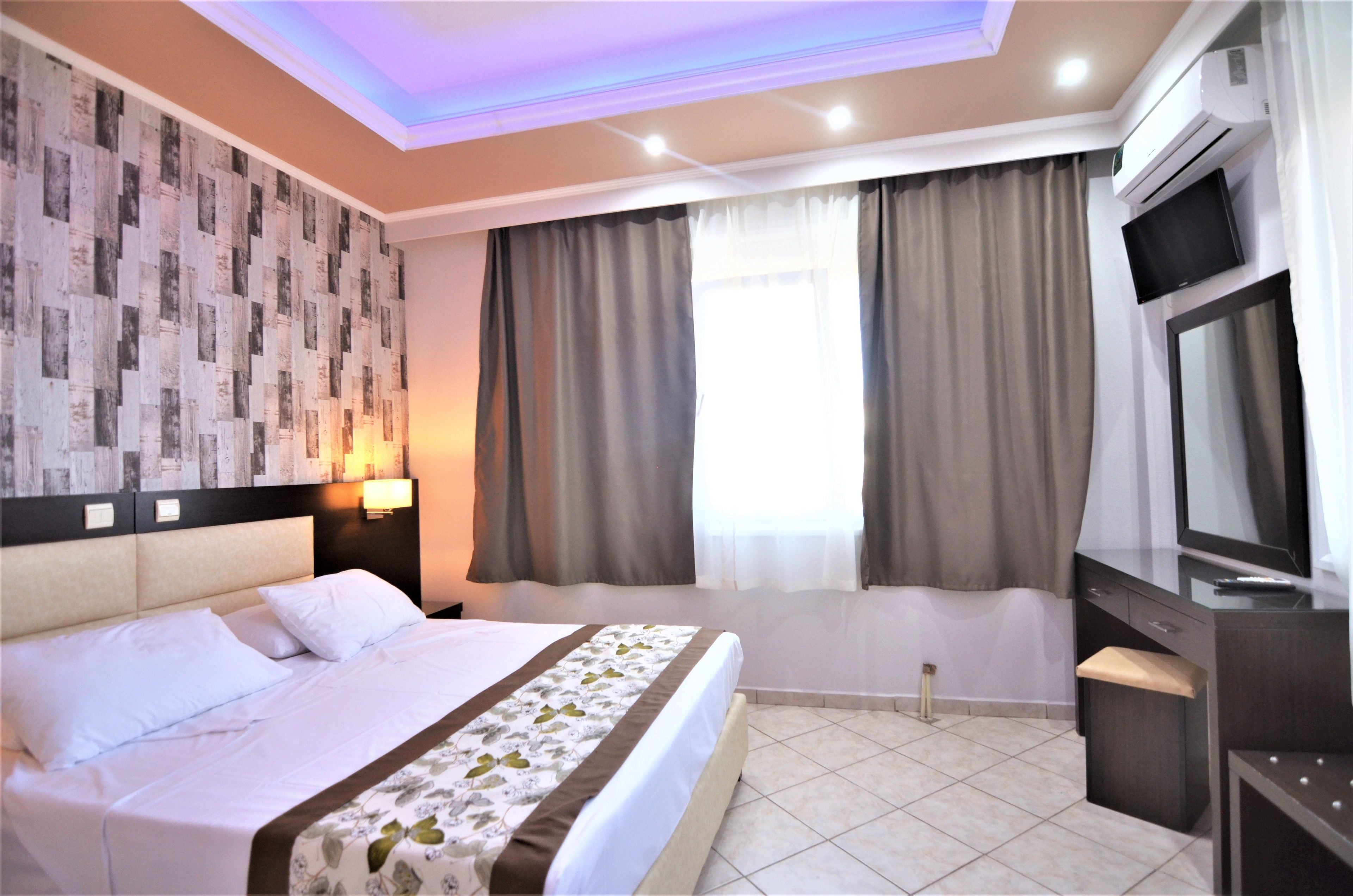 Quarto de hotel com cama, televisão, ar condicionado e janela com cortinas.