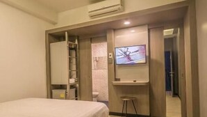 Quarto de hotel moderno com cama grande, roupeiro embutido, televisão de tela plana e um banquinho.