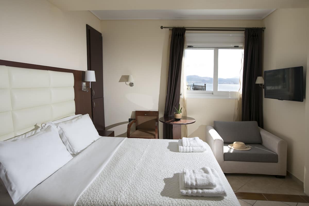 Quarto de hotel com cama, poltrona, mesa pequena, televisão e janela com cortinas.