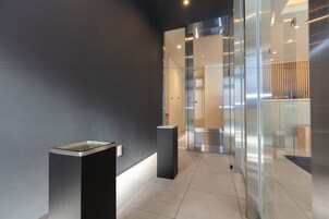 Um hall moderno com divisória de vidro, balcão de recepção e escada que dá acesso a um elevador.