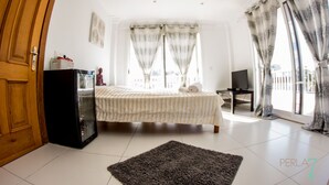 Quarto com cama, televisão, guarda-roupa e janela com cortinas.