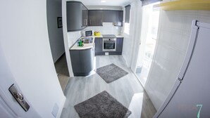 Uma cozinha compacta com armários cinza, um micro-ondas, uma pia e um fogão. Há dois tapetes no chão e uma janela que oferece luz natural.