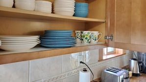 Uma cozinha com prateleiras de madeira exibindo tigelas brancas e azuis, uma caneca branca com desenho floral e uma torradeira no balcão.