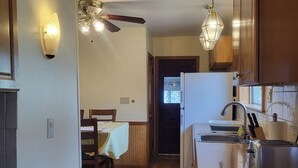 Uma cozinha com armários de madeira, uma mesa de jantar com cadeiras, um ventilador de teto e uma geladeira.