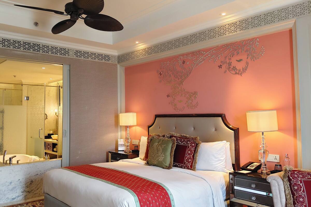 Quarto de hotel com cama grande, duas luminárias de cabeceira, ventoinha no teto e um mural decorativo na parede.