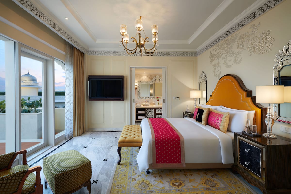 Quarto de hotel com uma cama grande, área de estar, televisão e vista para uma estrutura em forma de cúpula.