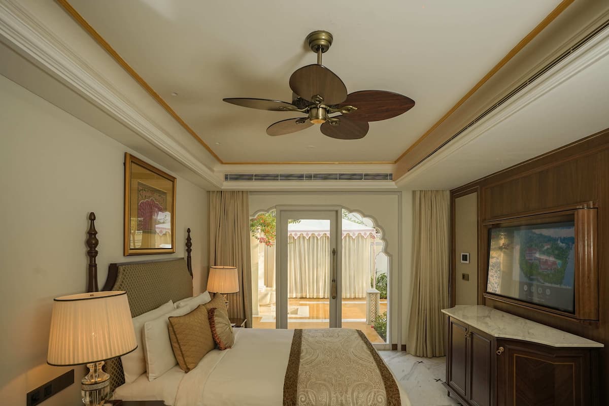 Quarto de hotel com cama, ventoinha no teto, televisão e vista para o exterior.