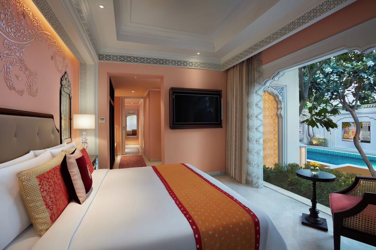 Quarto de hotel com uma cama grande, televisão, vista para a piscina e área de refeições com mesa e cadeira.