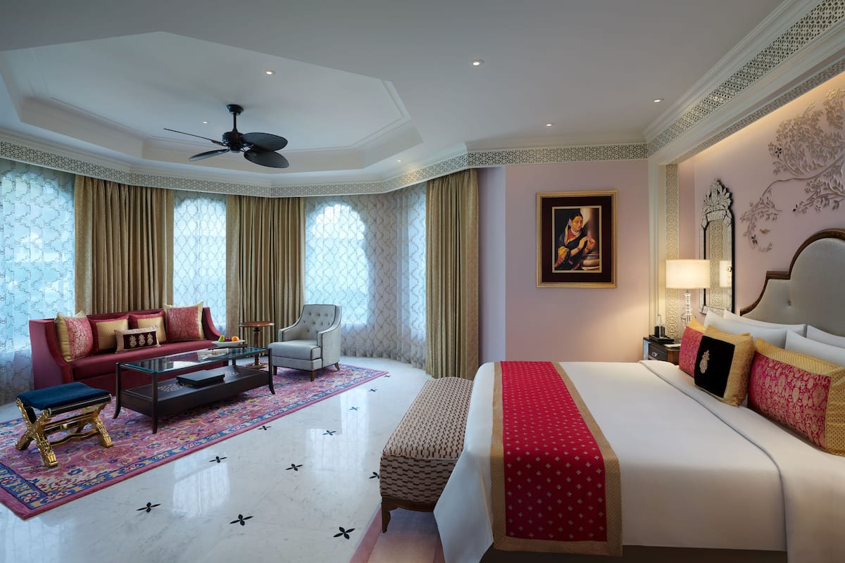 Quarto de hotel com cama grande, sofá, mesa de centro, poltrona e ventoinha no teto.