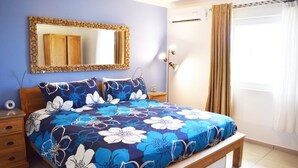 Quarto com cama, mesa de cabeceira, espelho, abajur e janela com cortinas.