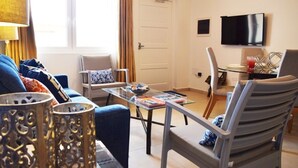 Uma sala de estar com sofá, poltronas, mesa de centro e TV fixada na parede.