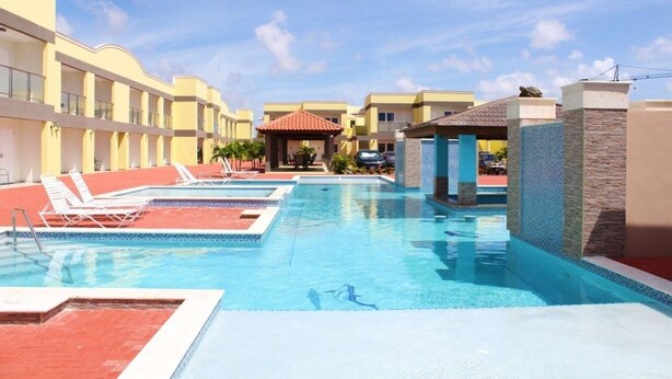 Piscina com espreguiçadeiras, área de estar coberta e um edifício com fachada em azulejos.