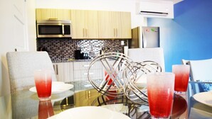Uma área de refeições com mesa de vidro, cadeiras de metal e bebidas vermelhas.